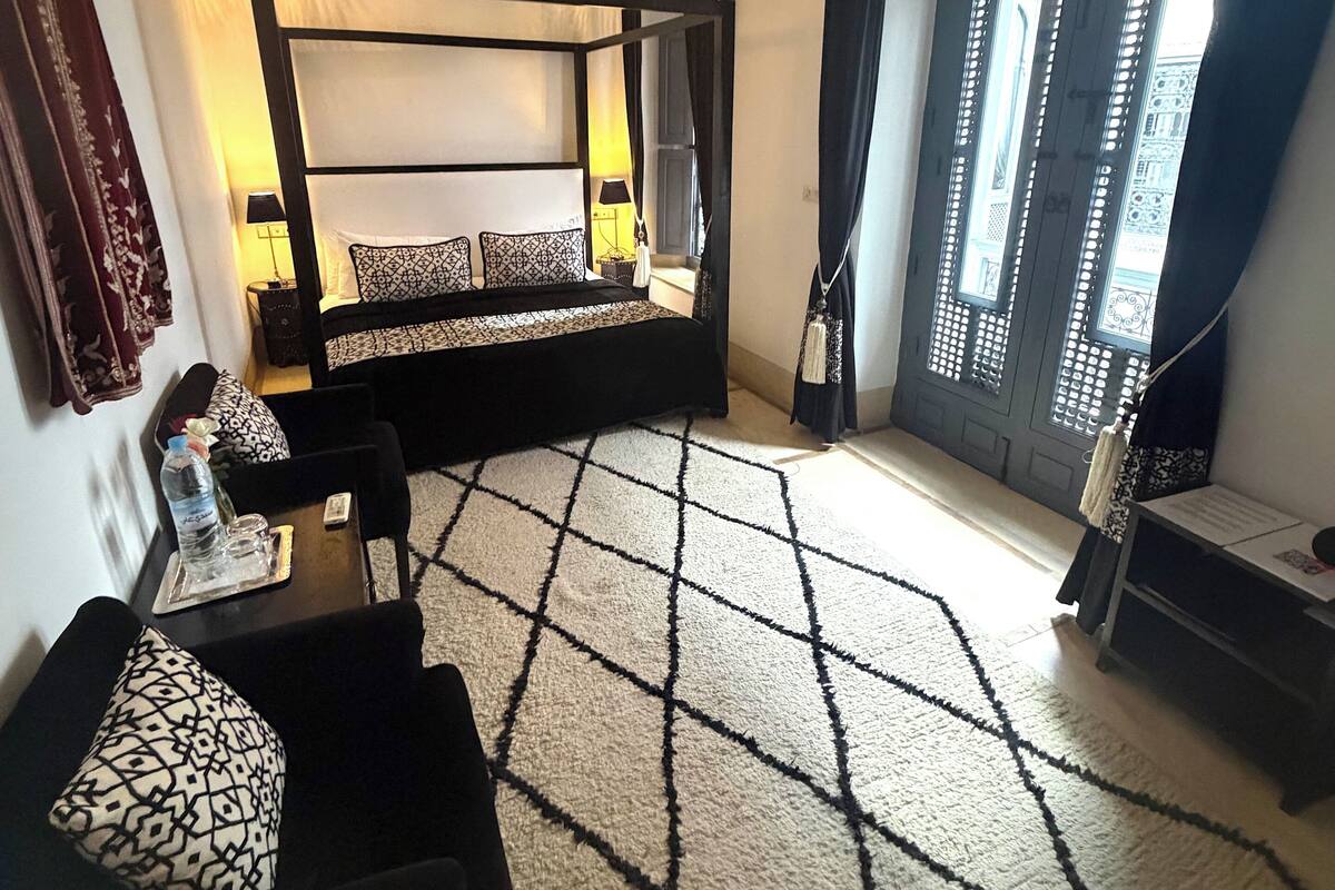 Quarto com uma cama de dossel, um sofá, uma mesa de centro e um tapete estampado.