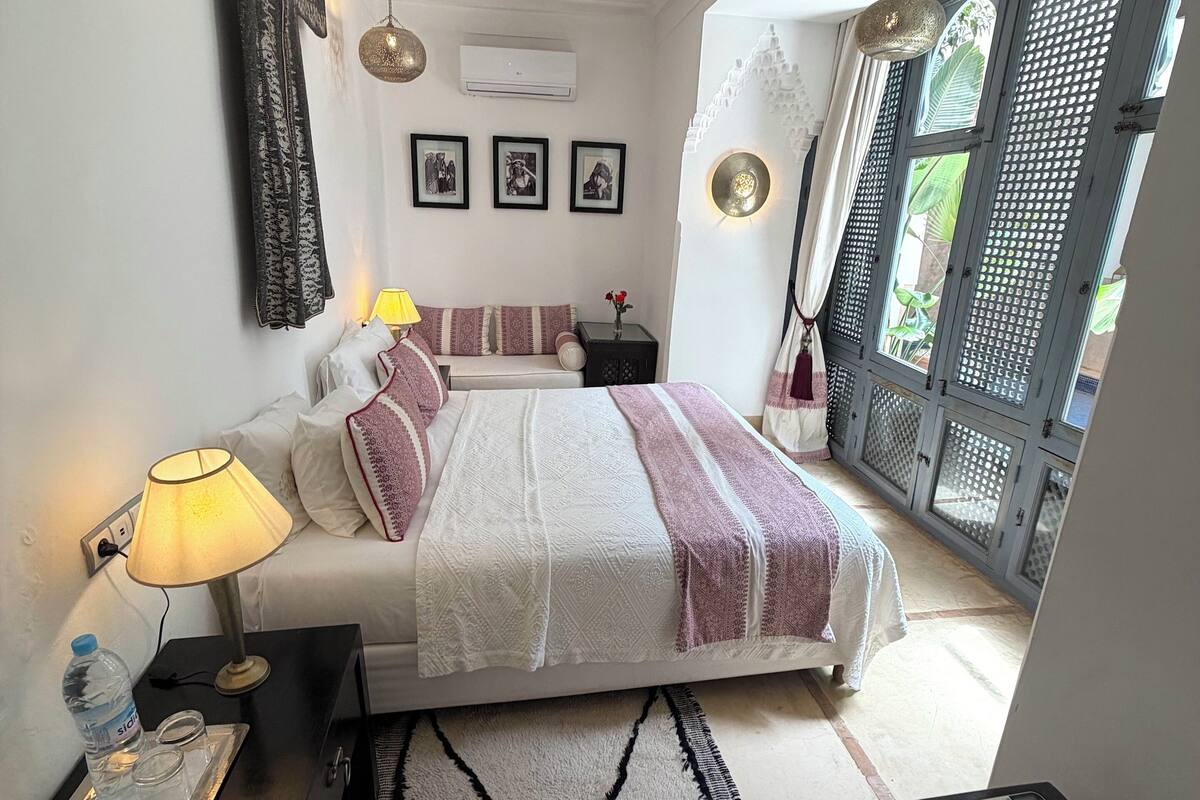 Quarto com cama, mesas de cabeceira, luminária, garrafa de água e tapete decorativo.