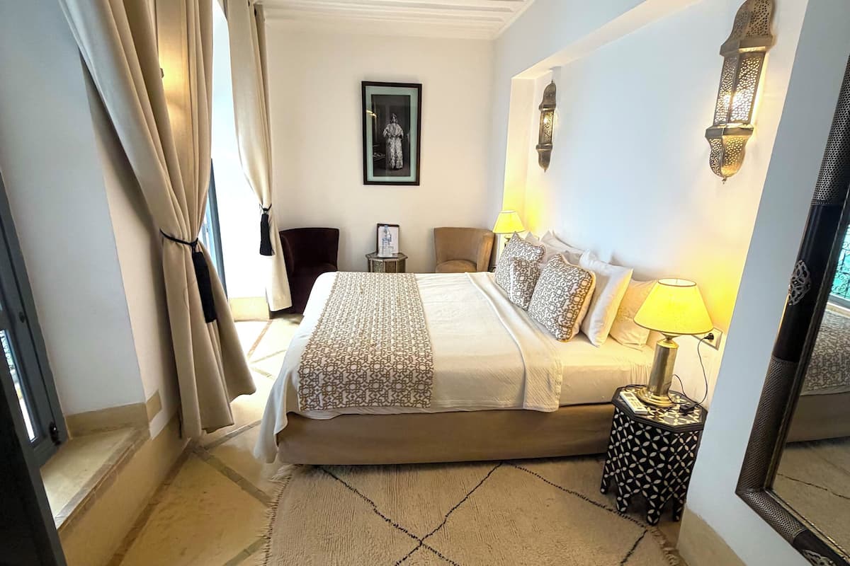 Quarto com cama, abajures, tapete, quadro emoldurado na parede e porta com cortinas.