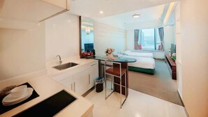 Quarto de hotel compacto com cozinha compacta, uma pequena mesa de jantar, uma cama e uma janela com vista para a cidade.