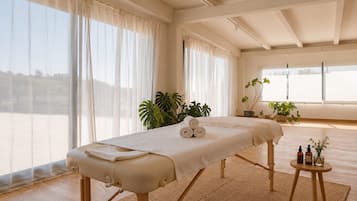 Sala de spa com mesa de massagem, janelas amplas e plantas em vasos.