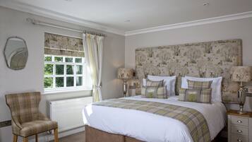Quarto com cama grande, uma cadeira, mesa de cabeceira e janela com cortinas.