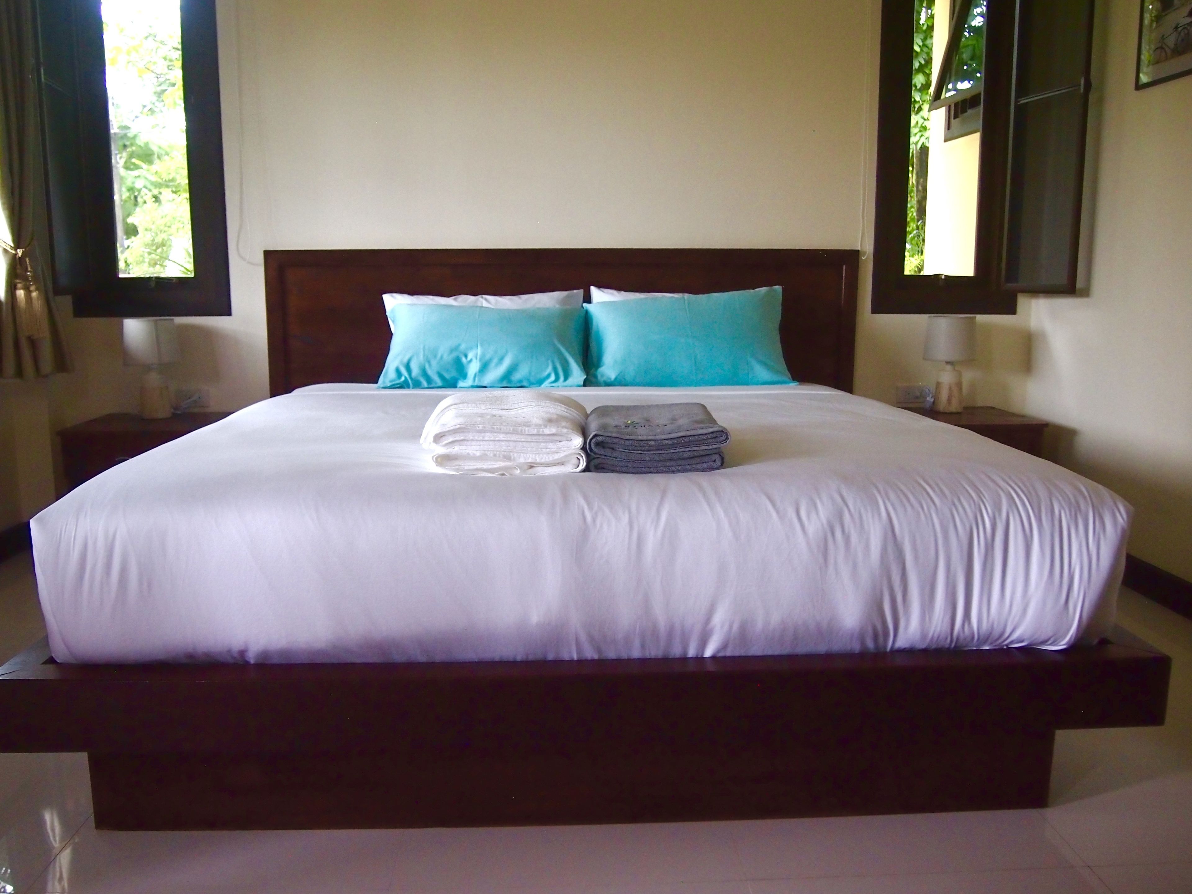Uma cama bem arrumada com roupa de cama branca e azul, uma cabeceira de madeira e duas luminárias de mesa.