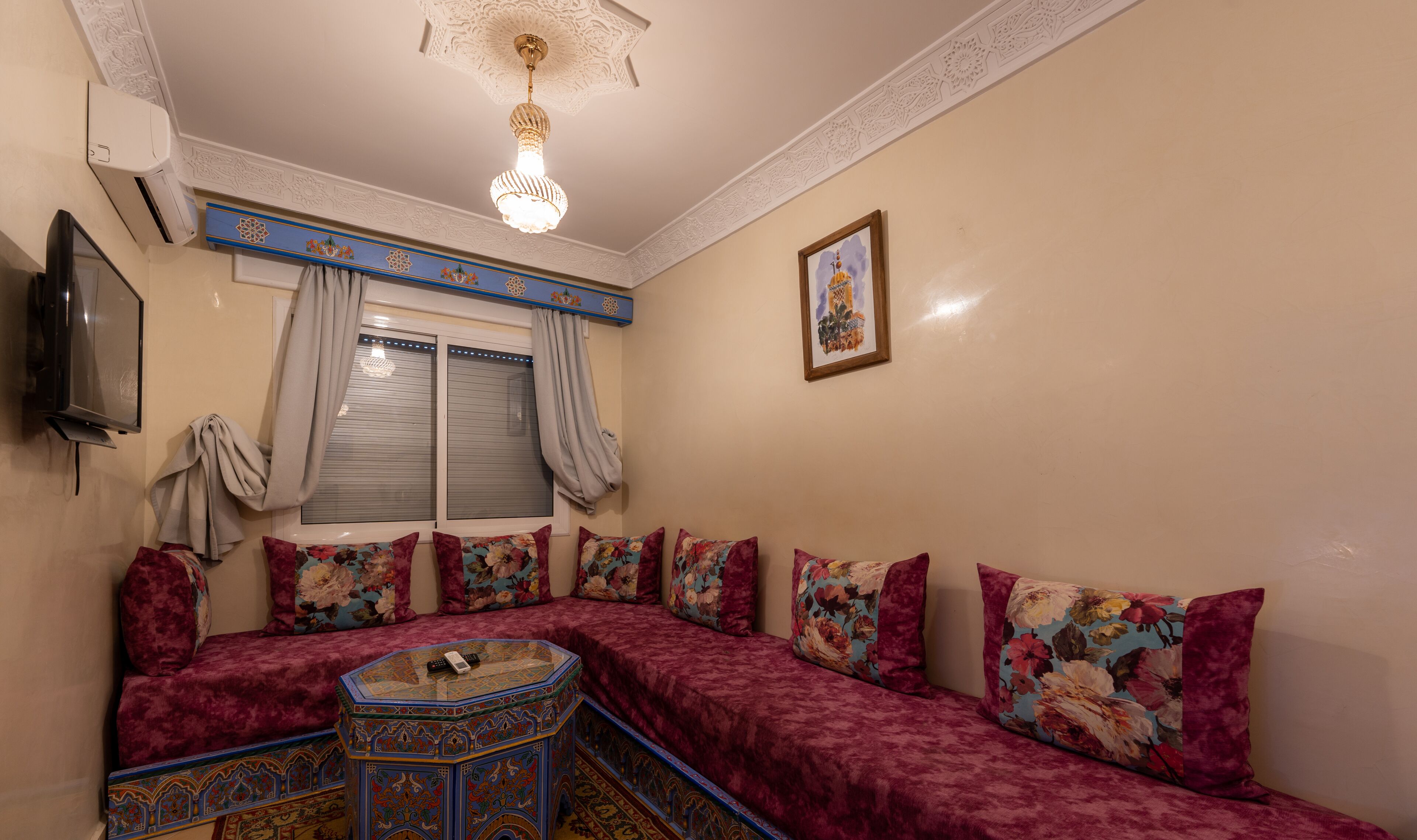 Quarto com sofá, televisão, luminária decorativa no teto e janela com cortinas.