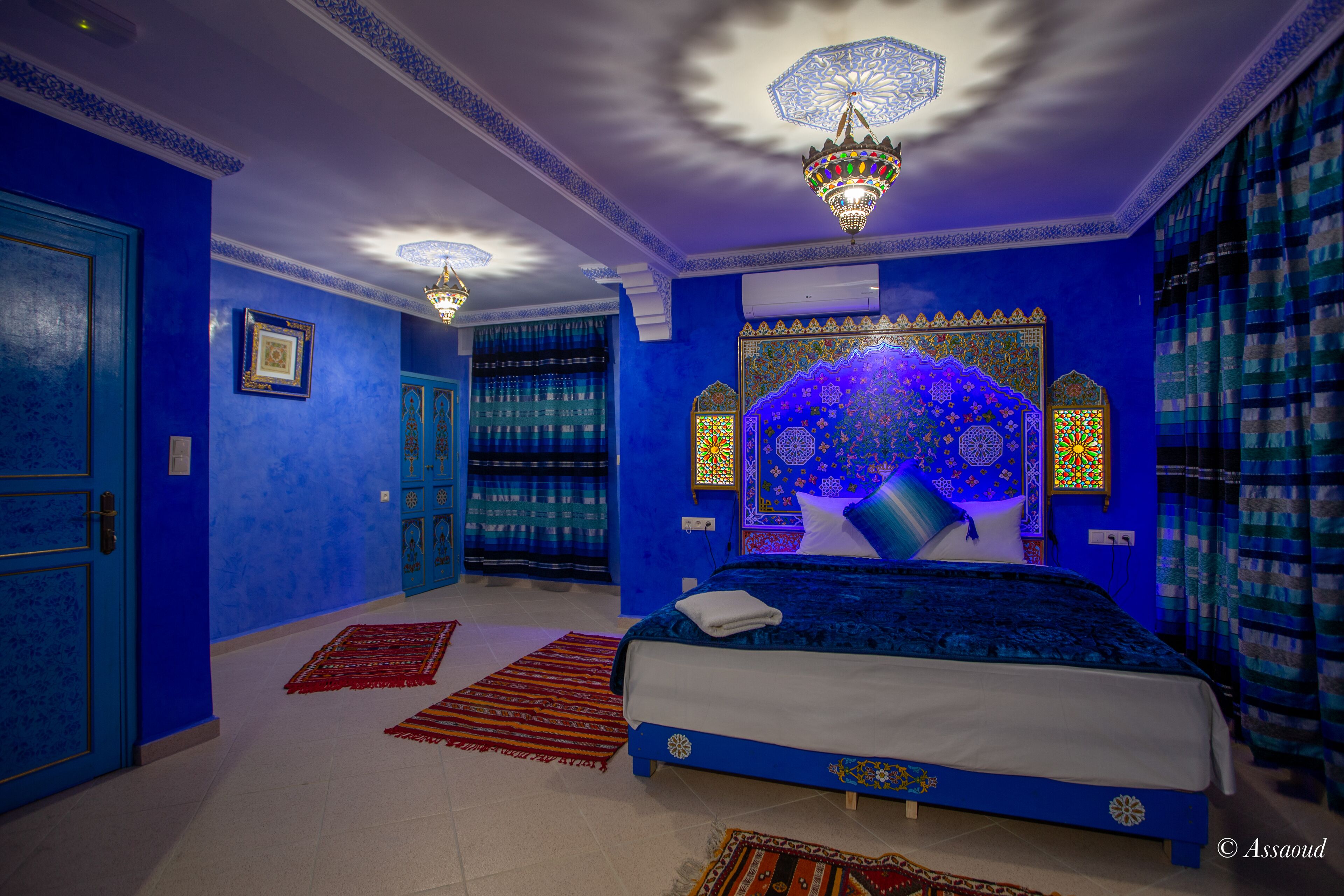 Quarto com cama grande, paredes azuis e decoração detalhada nas paredes.