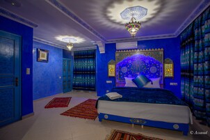 Quarto com cama grande, paredes azuis e decoração detalhada nas paredes.