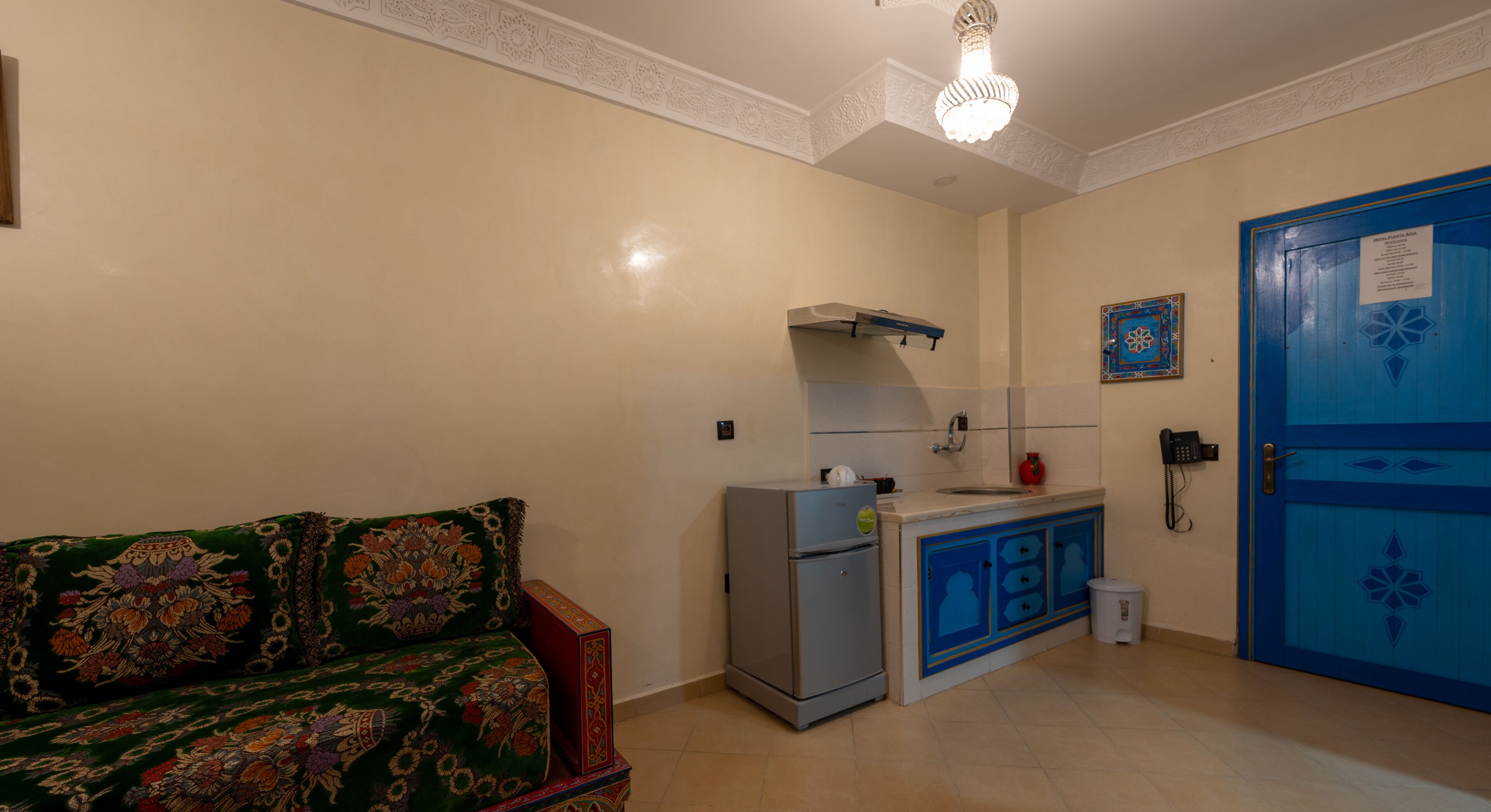 Um espaço compacto com sofá, cozinha compacta, porta azul e parede estampada.