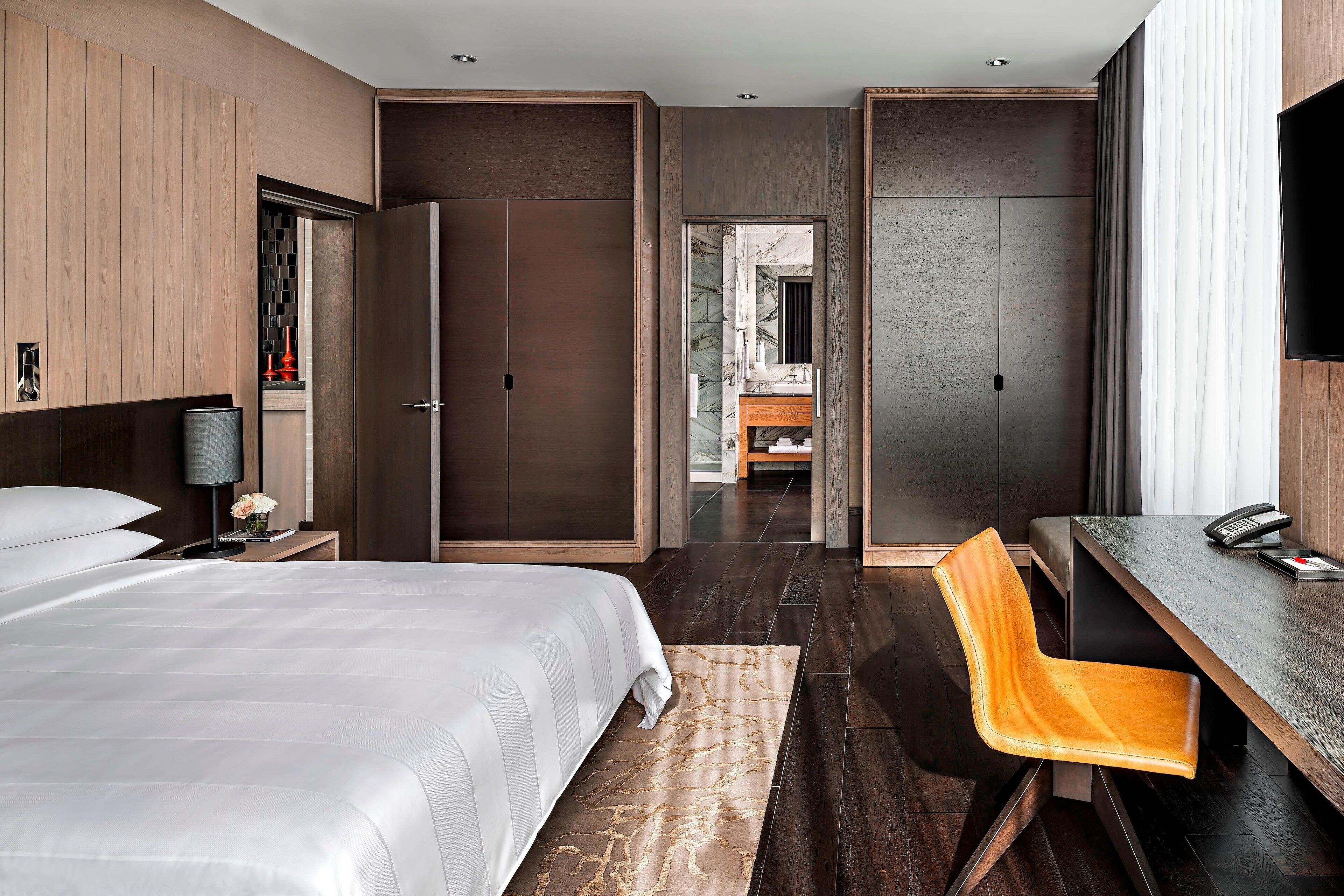 Quarto de hotel moderno com uma cama grande, uma escrivaninha com cadeira e uma televisão.
