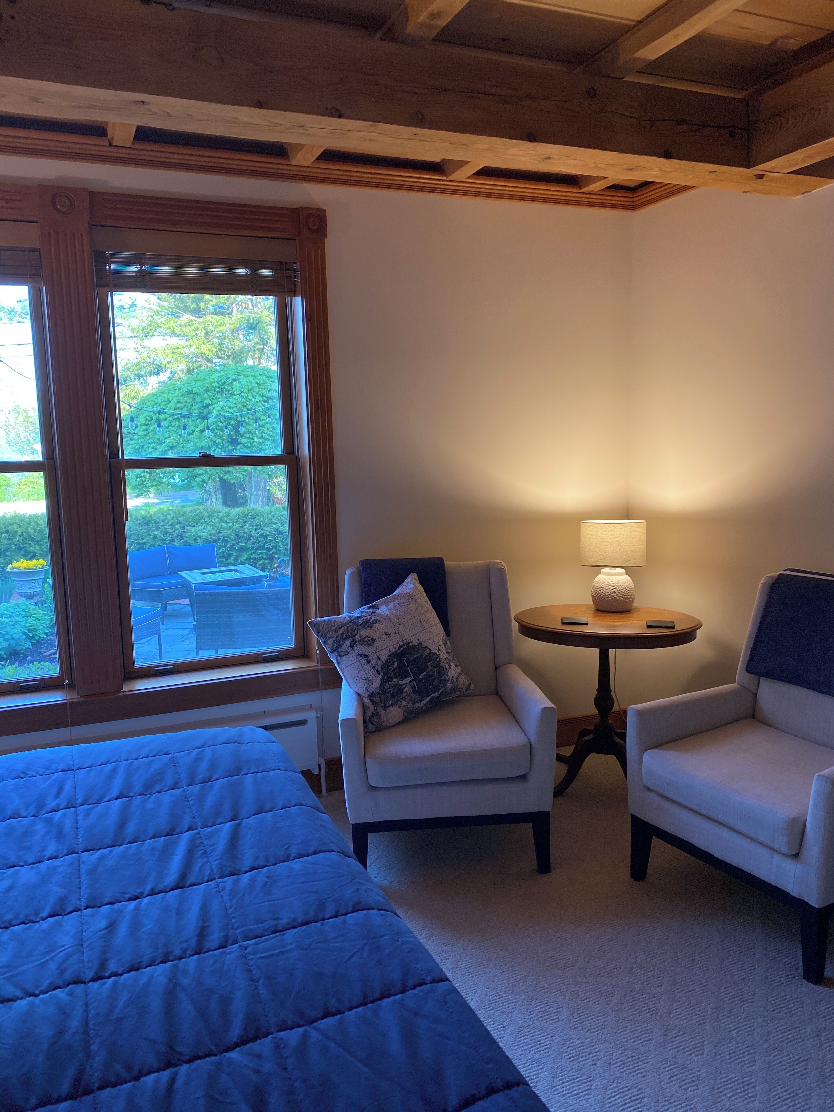 Quarto com uma cama, duas poltronas, uma mesinha com abajur e janela com vista para vegetação.