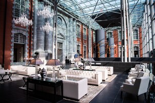 Um hall de entrada luxuoso, com pé direito alto, grandes lustres e arquitetura clássica.