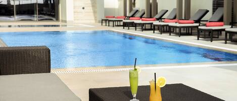 Uma área de piscina com espreguiçadeiras e duas bebidas sobre uma mesa.