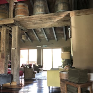 Um interior rústico com vigas de madeira, grandes barris e um espaço de estar com uma mesa e cadeiras amarelas.