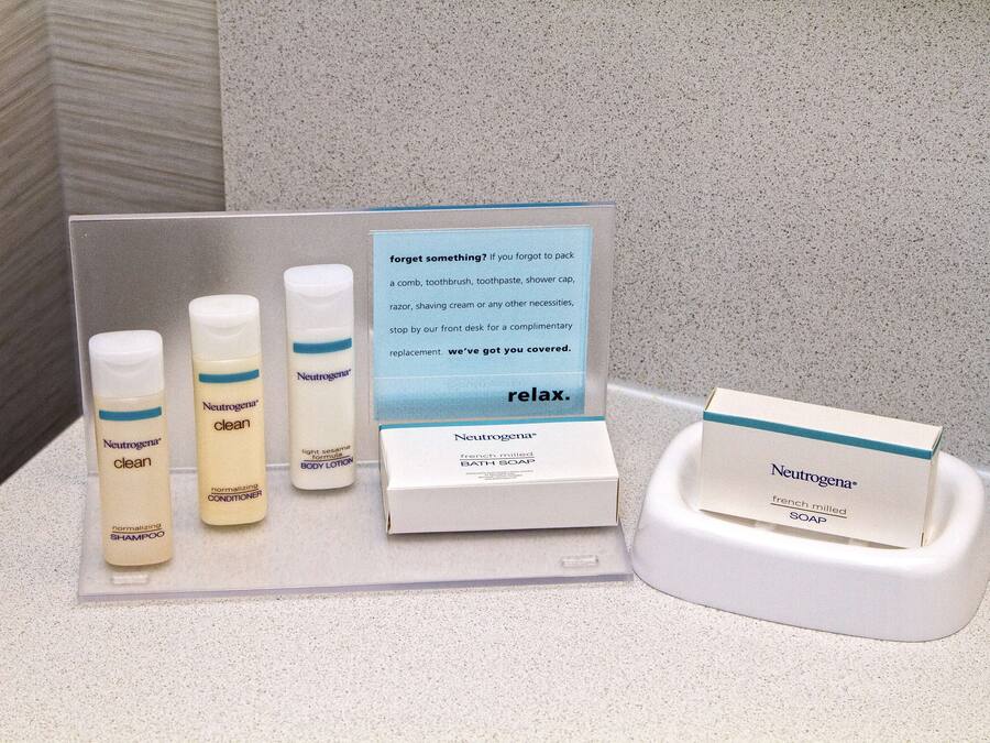 Exposição de produtos Neutrogena, incluindo shampoo, loção corporal e sabonete de banho, com um aviso oferecendo reposições gratuitas para itens esquecidos.