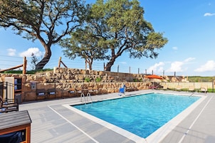 Piscina retangular com muro de pedra e espreguiçadeiras ao redor.