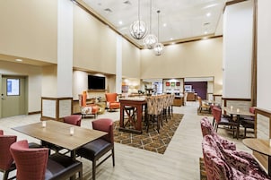 Um hall de hotel com diferentes espaços de estar, um bar e uma tela de televisão.
