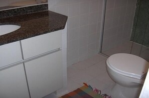 Casa de banho com uma pia branca, sanita branca e zona de duche.