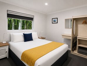 Quarto de hotel com cama, mesas de cabeceira, guarda-roupa e janela com vista para o verde.