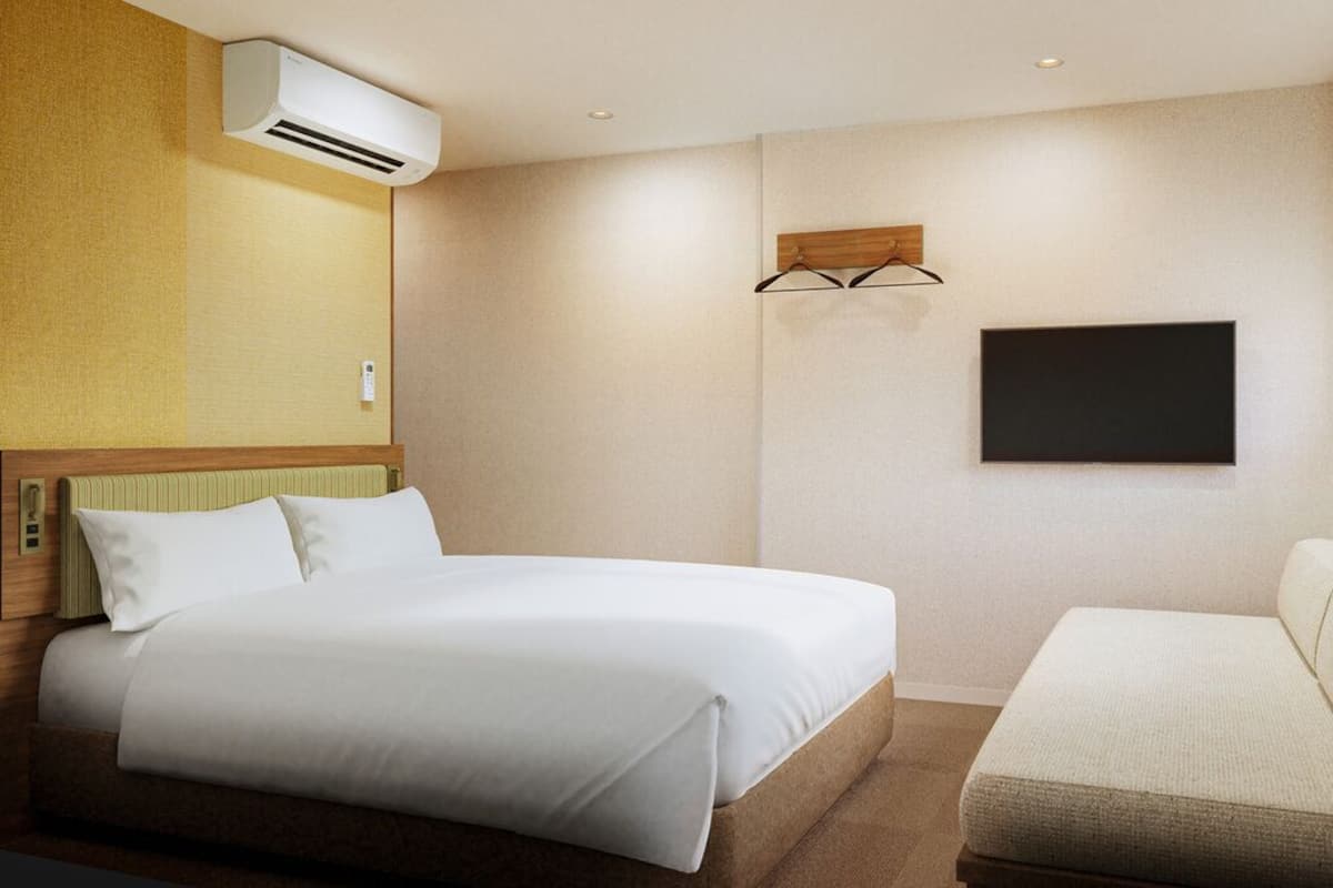 Quarto de hotel com cama, sofá, ar condicionado, televisão fixada na parede e janela.