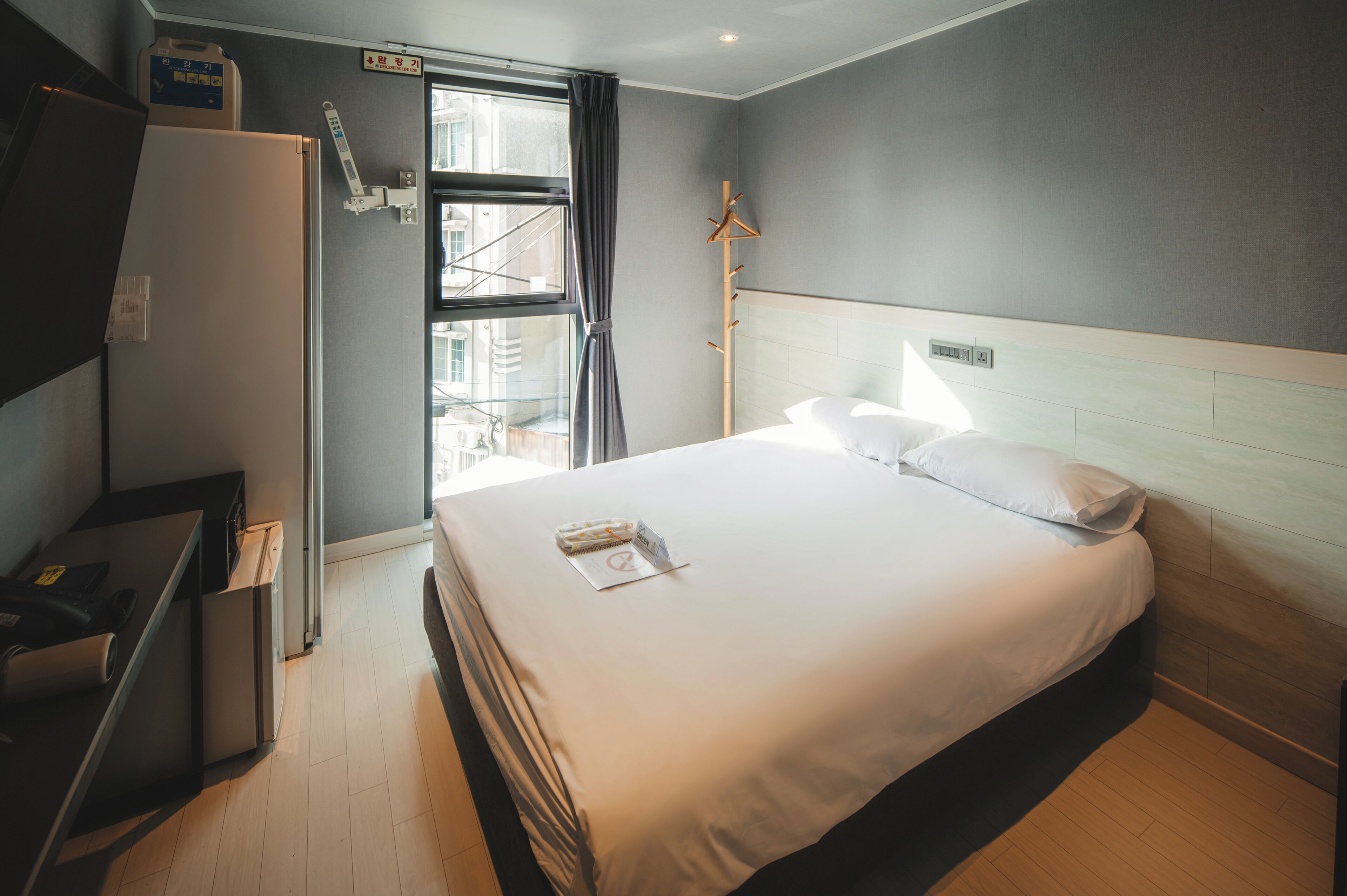 Quarto de hotel com cama, escrivaninha, frigorífico e janela com cortinas.