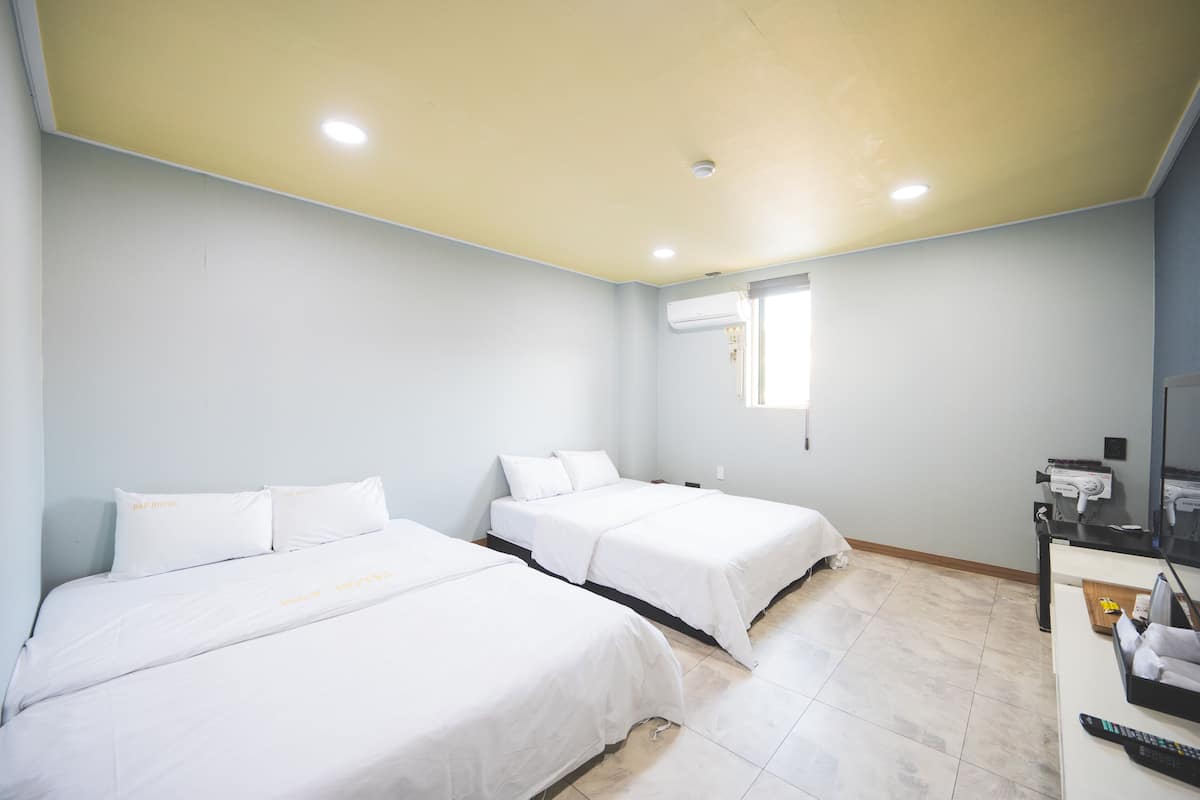 Quarto de hotel com duas camas, uma escrivaninha com computador e uma janela.