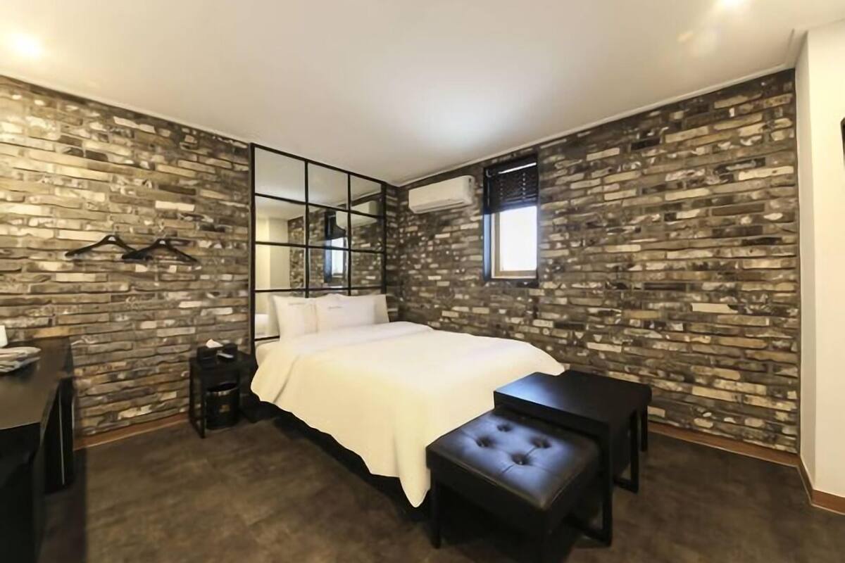 Quarto com parede em padrão de pedra, uma cama, uma escrivaninha e uma janela.
