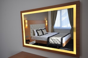 Quarto de hotel moderno com um espelho grande, cabeceira estofada, cama bem arrumada e mesa de cabeceira.