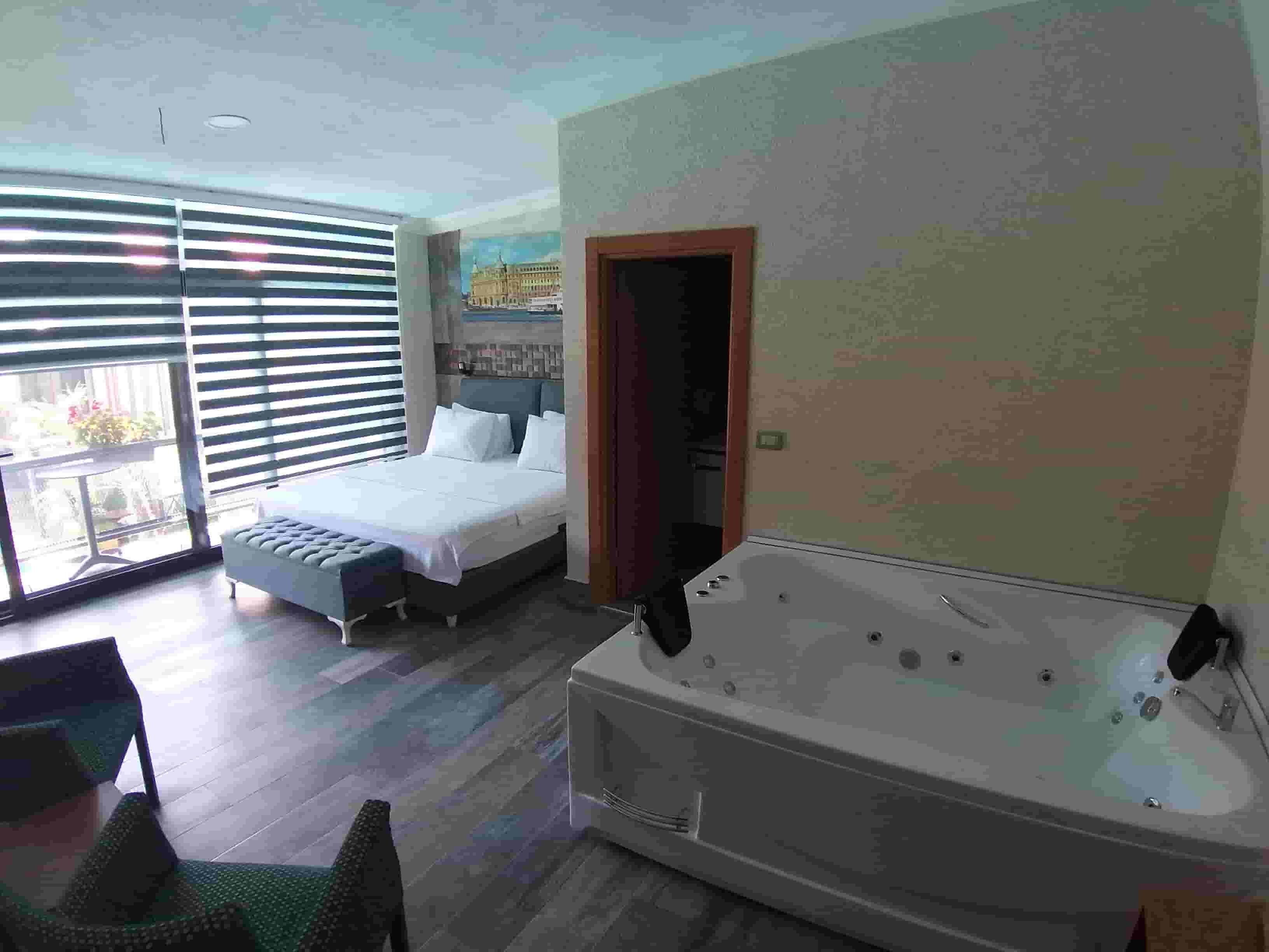 Quarto com uma cama grande, área de estar com uma poltrona, banheira e vista para um edifício.