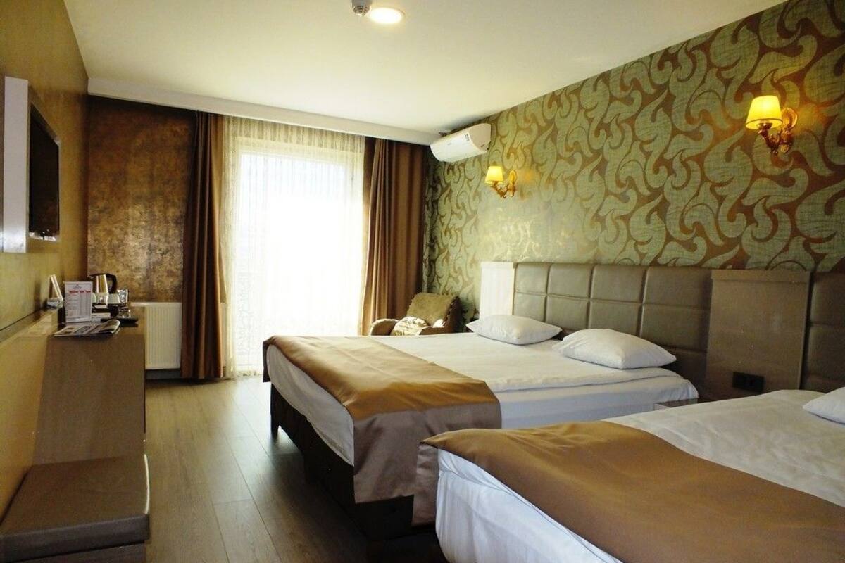 Quarto de hotel com duas camas, uma escrivaninha com telefone e uma televisão na parede.