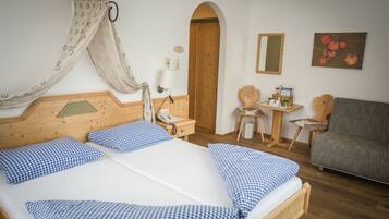 Um quarto com uma cama grande, cabeceira de madeira, mesa de cabeceira com abajur, uma cadeira de madeira pequena, um sofá cinza e uma porta de madeira com arco.