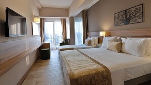 Quarto de hotel com uma cama grande, televisão, escrivaninha e varanda com cortinas.