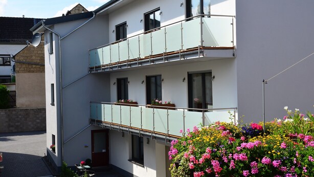 Um edifício moderno de dois andares com varandas, antena parabólica e caixas de flores.