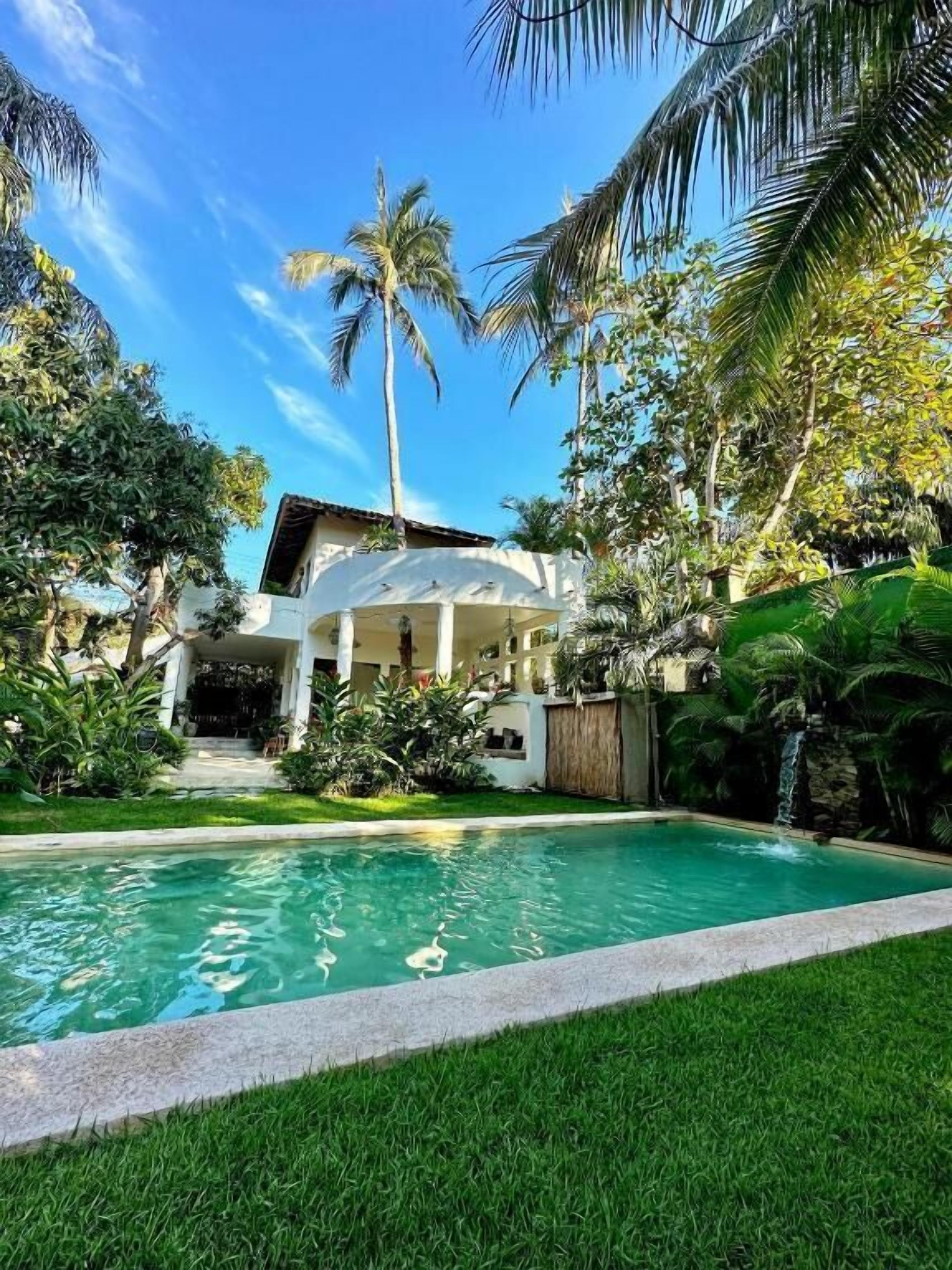 Piscina cercada por vegetação exuberante e um edifício com varanda coberta.