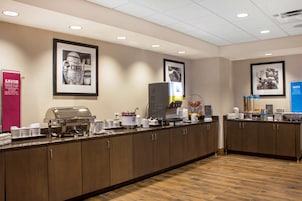 Buffet montado com diversas estações de comida, uma máquina de café e quadros nas paredes.
