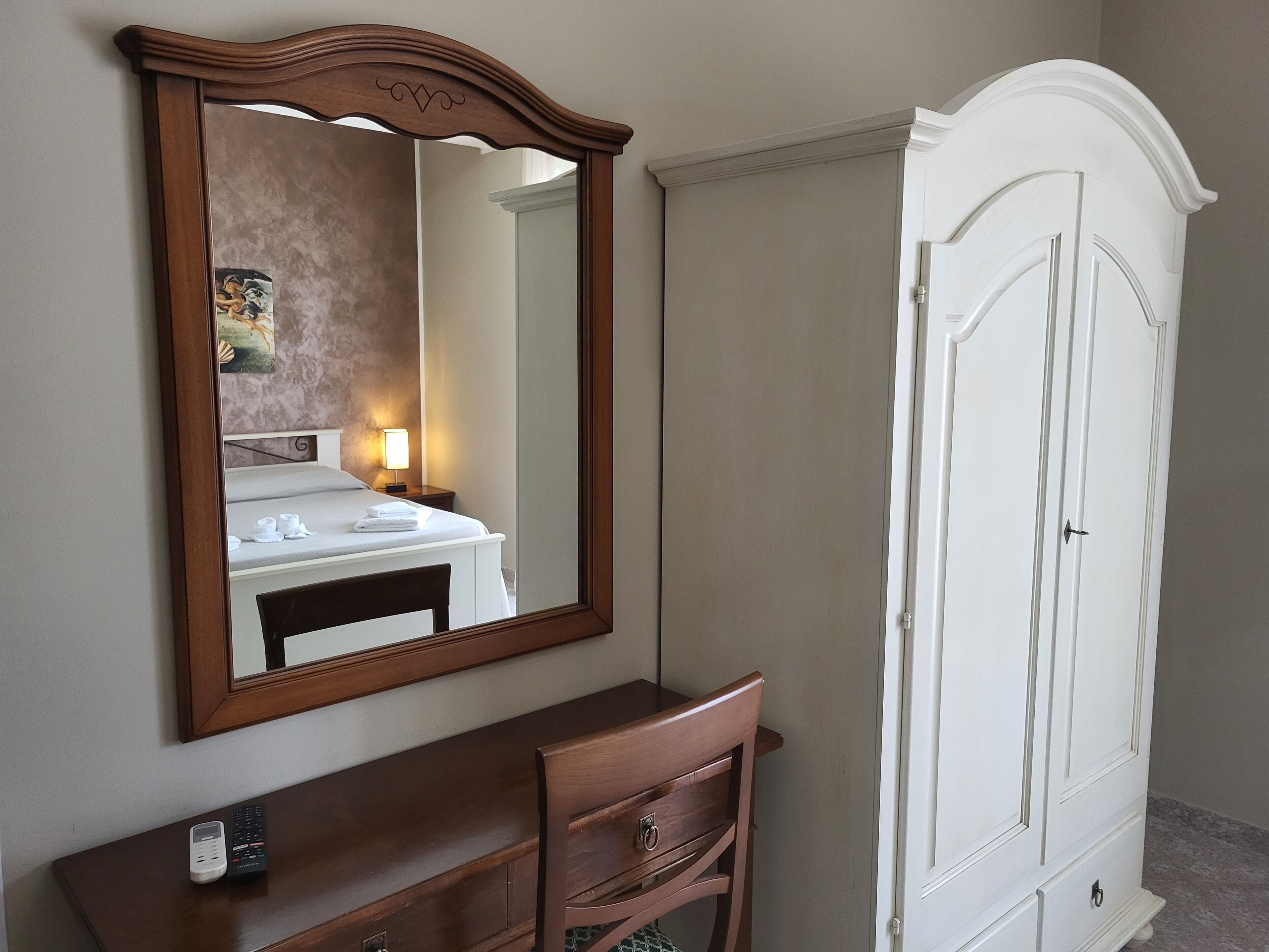 Quarto de hotel com um espelho grande, cómoda de madeira e guarda-roupa branco.