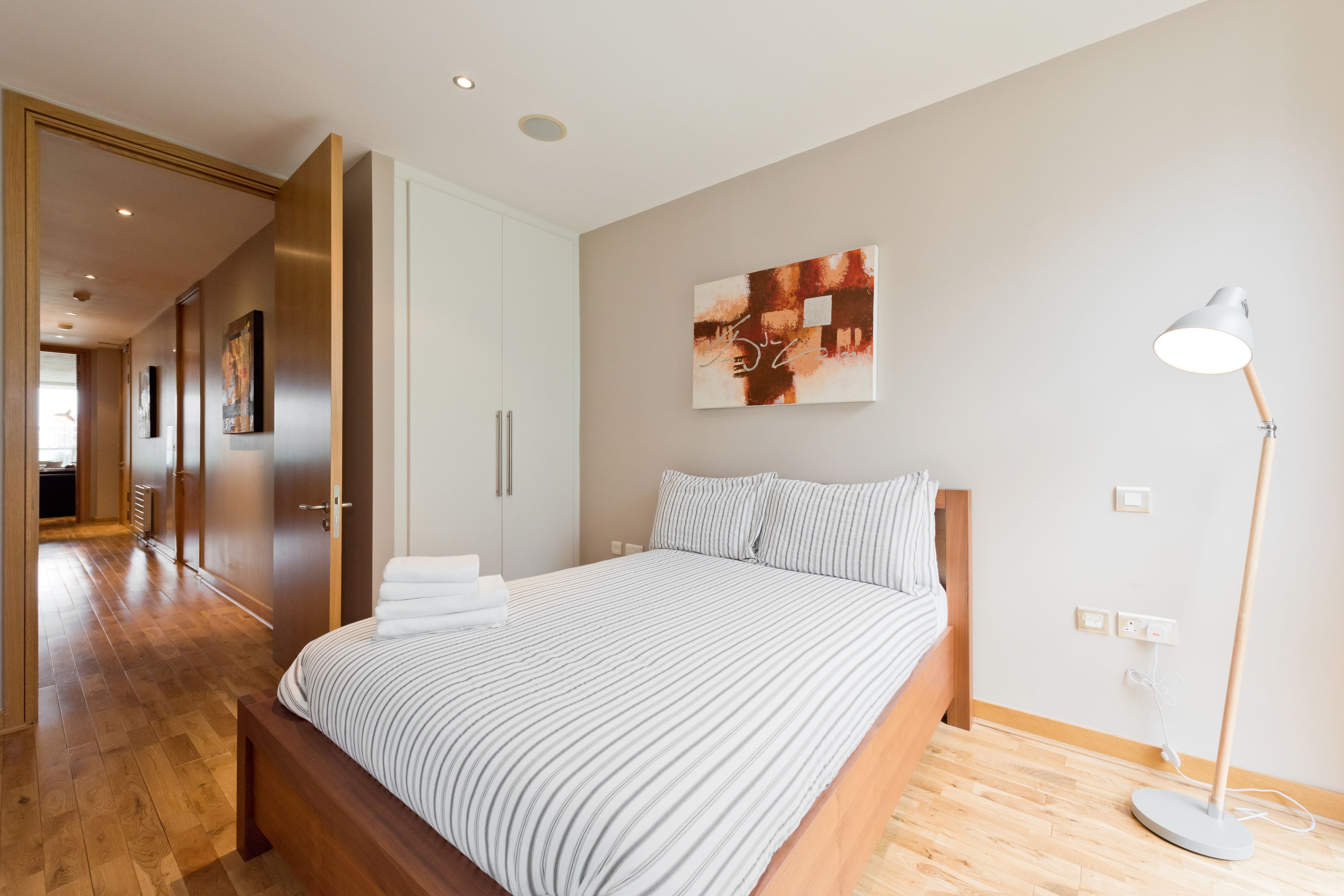 Quarto moderno com uma cama grande, piso de madeira, um abajur e um quadro na parede.