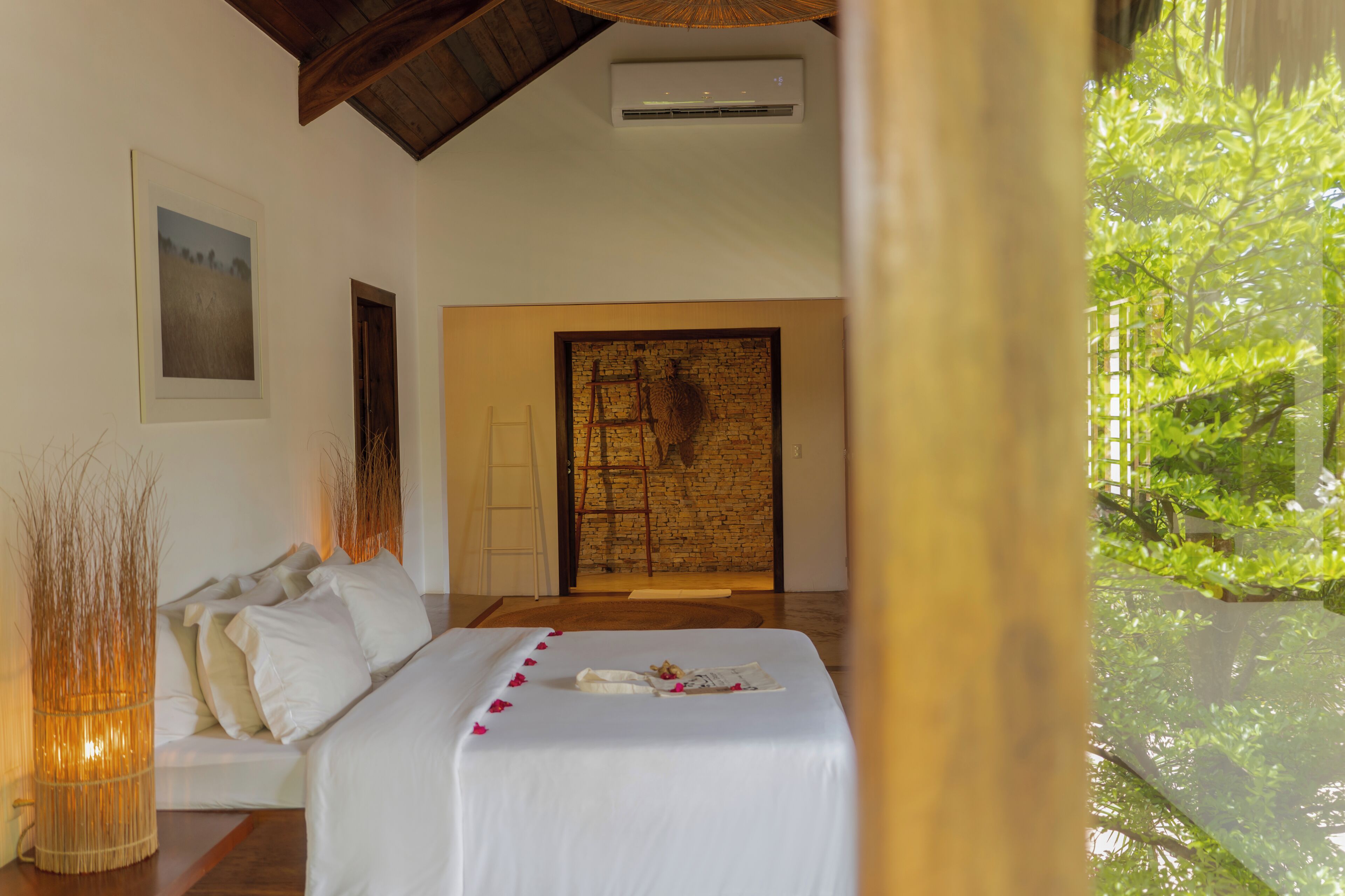 Quarto com cama, quadro, escada e parede de pedra.