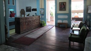 Uma área de recepção com balcão de madeira, porta com moldura azul, uma pintura e vista para o exterior.