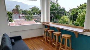 Uma varanda com piso de madeira, um sofá preto e banquinhos de madeira.