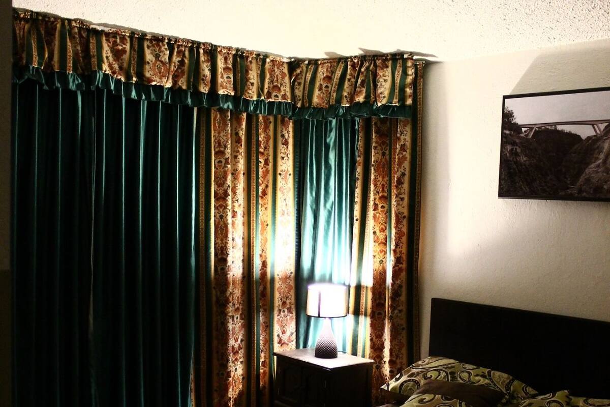 Quarto com cama, mesa de cabeceira, abajur e cortinas.