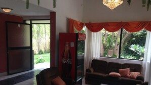 Uma sala de estar com sofá, poltronas, mesa de centro, televisão e refrigerador Coca-Cola.