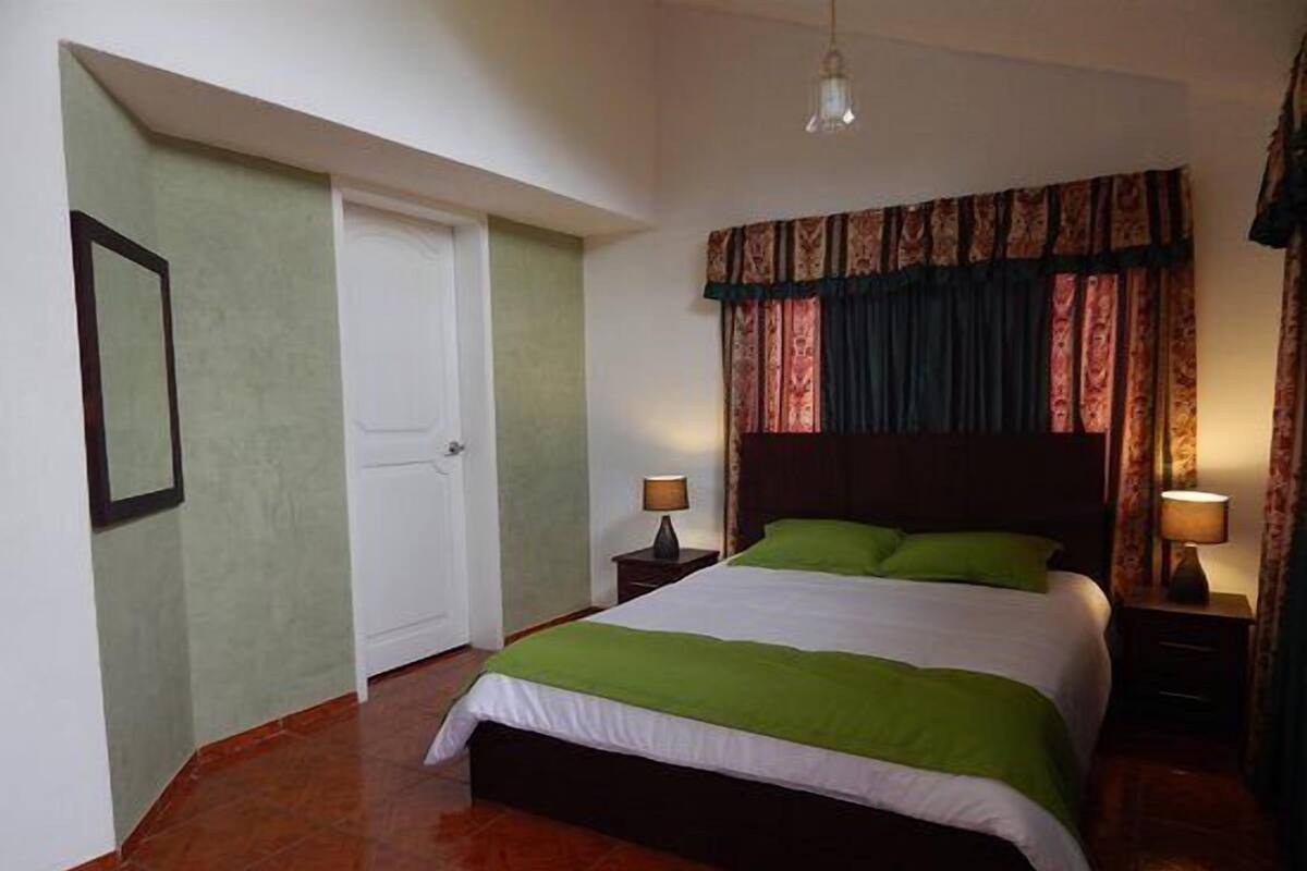 Quarto com cama, duas mesas de cabeceira, uma porta e um lustre.