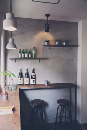 Uma área de bar com bancos de madeira, uma prateleira com garrafas e luminárias pendentes.