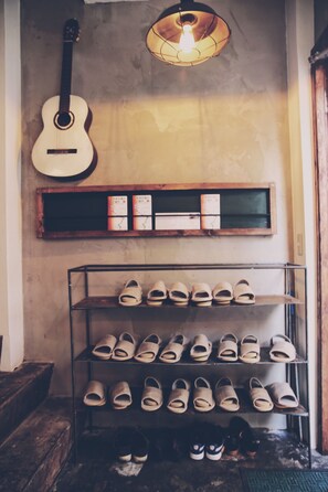 Uma parede com uma guitarra, uma estante com caixas de sapatos e um sapateiro com vários pares de sapatos.