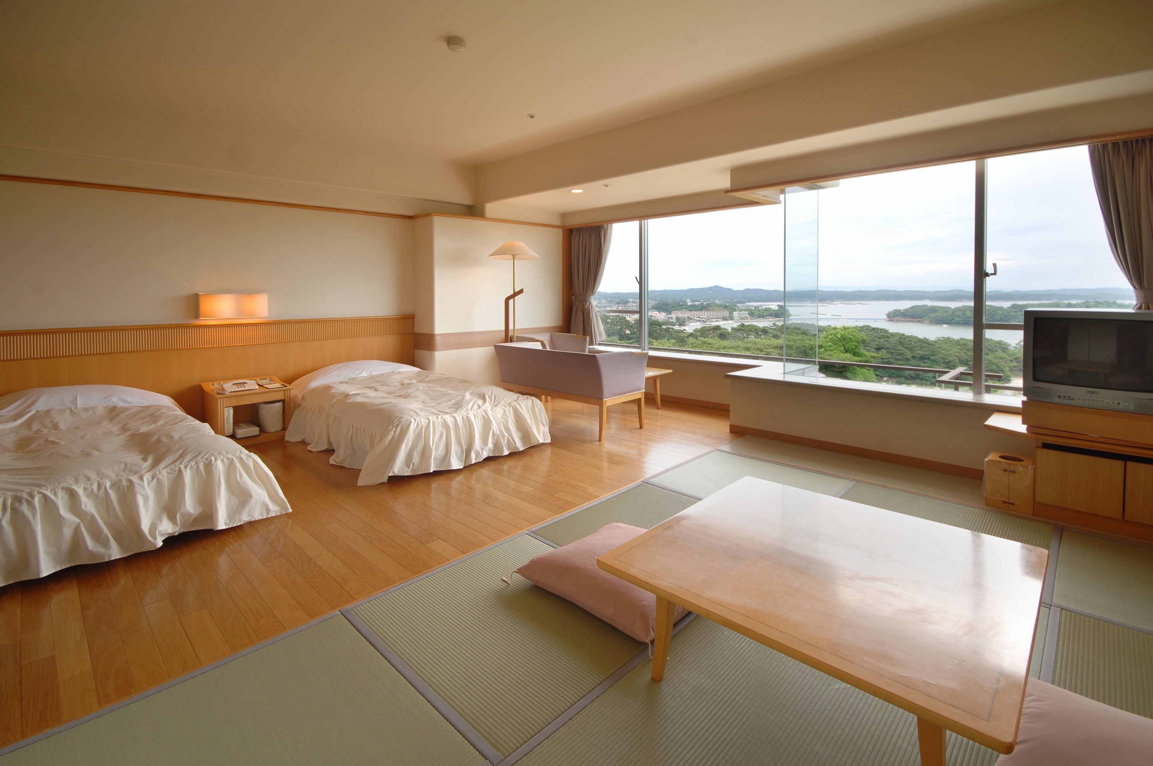 Quarto de hotel com duas camas, televisão, mesa e vista para a paisagem urbana.