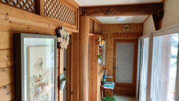 Interior em madeira com uma obra de arte emoldurada, uma estante com livros e uma porta com painel de vidro estampado.