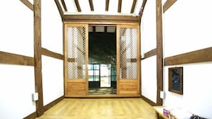 Quarto com piso de madeira, porta deslizante com vista e um pequeno banco com objetos em cima.