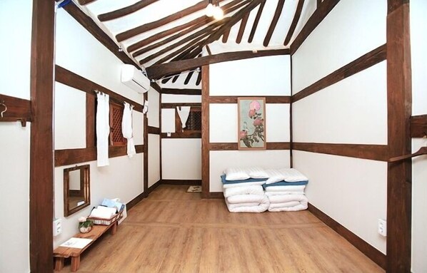 Quarto com vigas de madeira aparentes, um banco de madeira, um espelho e um quadro na parede.