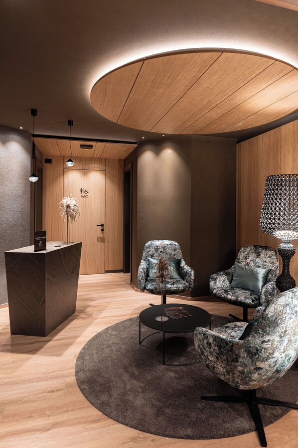 Um interior moderno com um balcão de recepção, duas poltronas estampadas, uma mesa de centro redonda e um design de teto singular.