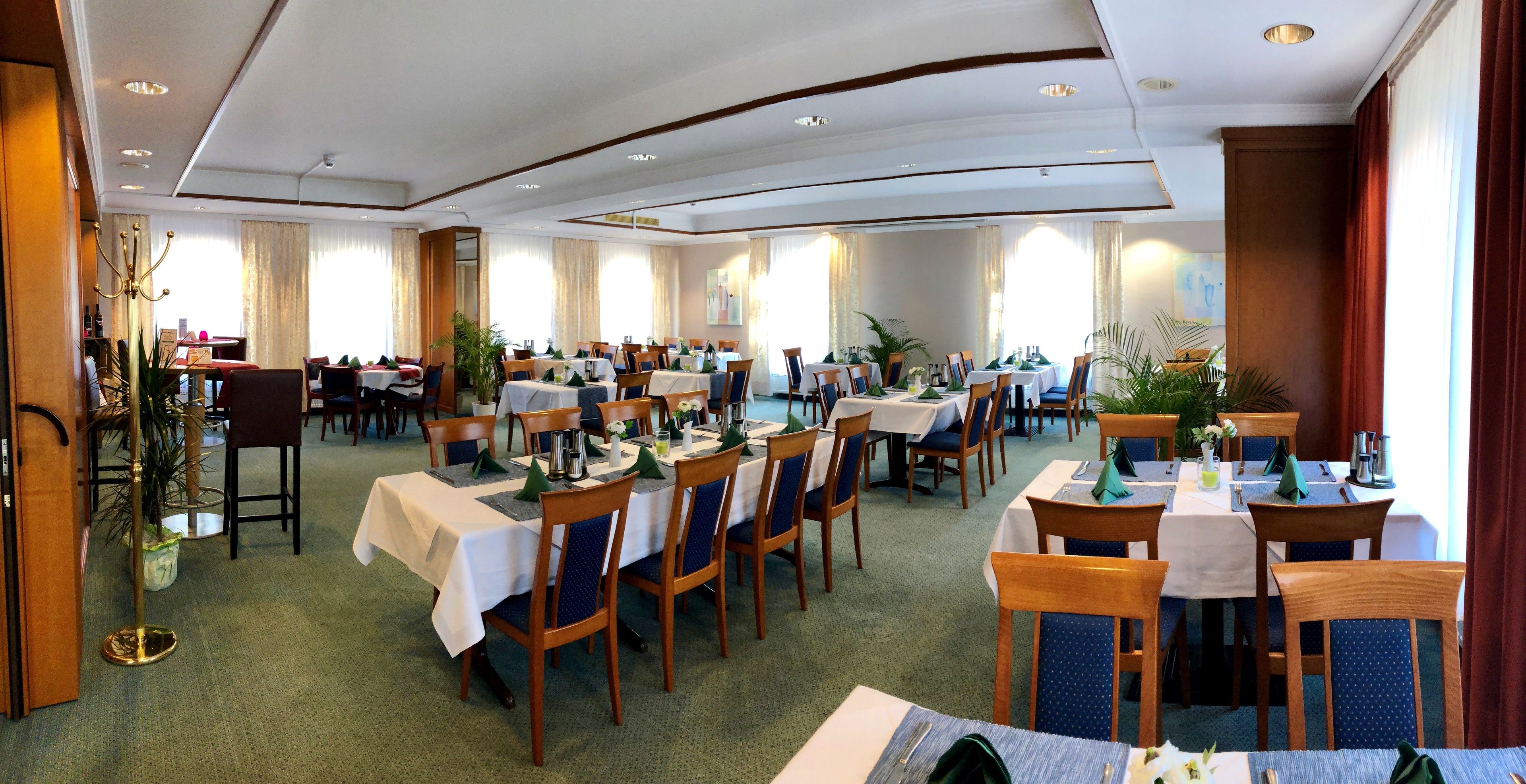 Uma sala de jantar de hotel com várias mesas e cadeiras, dispostas num espaço amplo.