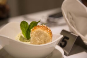 Uma tigela branca com um pedaço de pão coberto com sementes de gergelim e uma folha verde, colocada sobre uma mesa com uma placa de número 5.